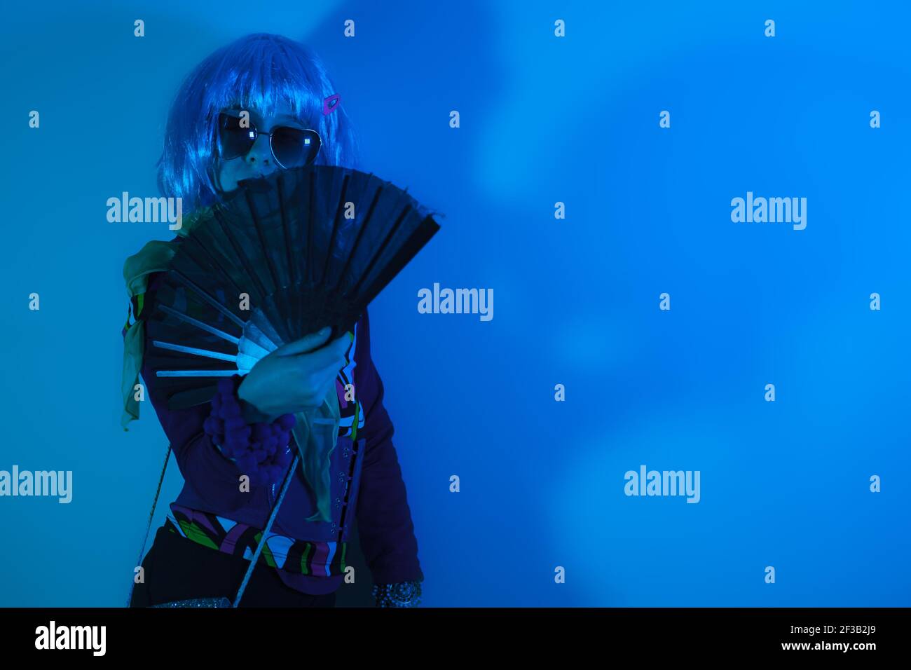 Little girl posing with a fan for a photo shoot on a blue background ...