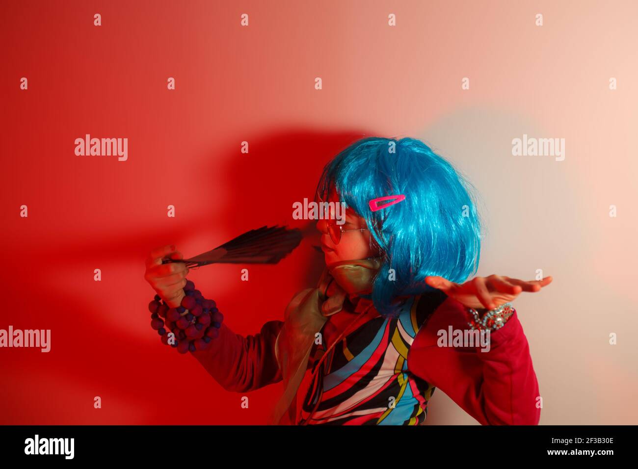 Little girl posing with a fan for a photo shoot on a red background ...