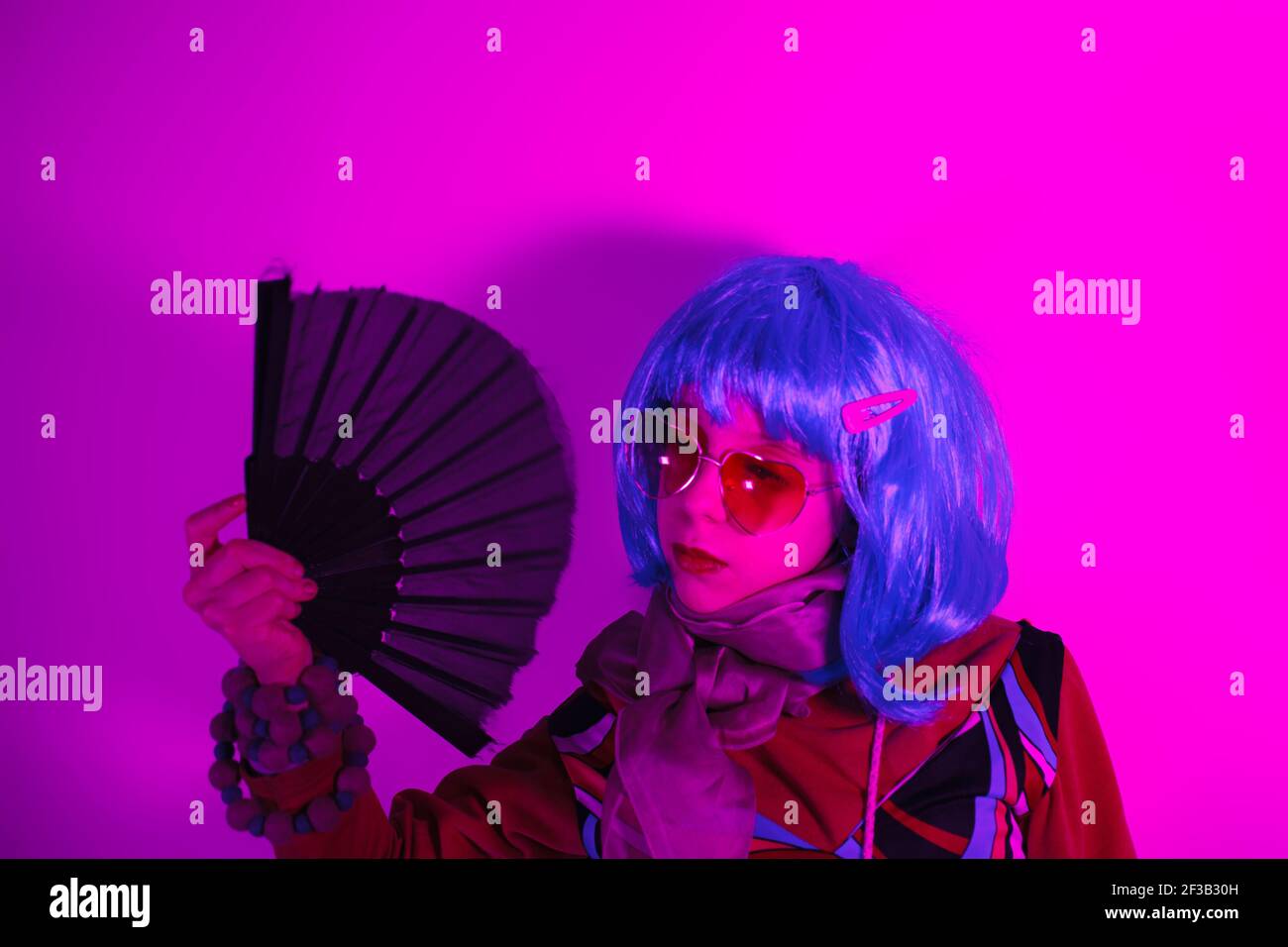 Little girl posing with a fan for a photo shoot on a fuchsia background ...
