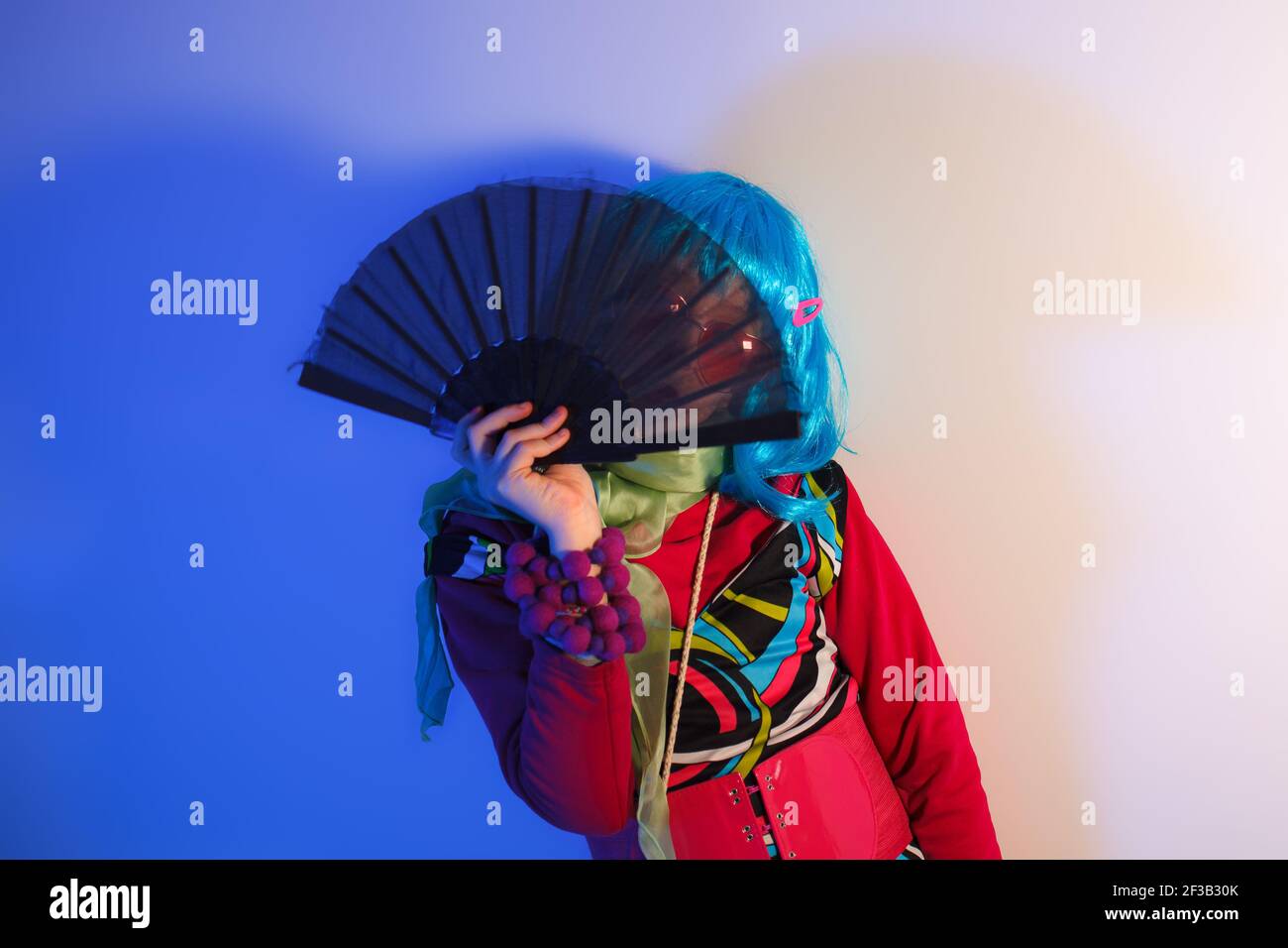 Little girl posing with a fan for a photo shoot on a blue background ...