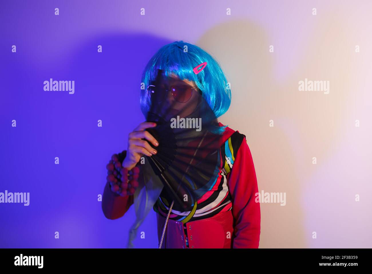 Little girl posing with a fan for a photo shoot on a purple background ...