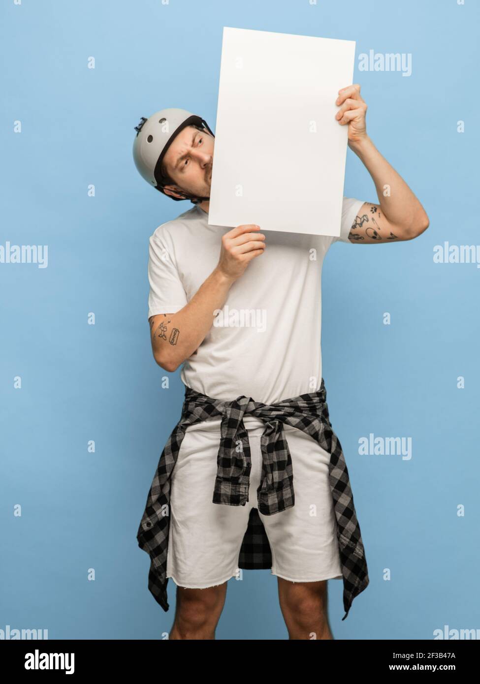 Young shocked man with blank sheet of paper isolated on blue background ...