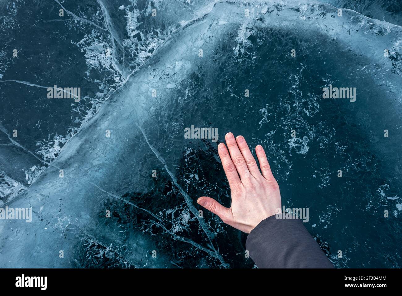A woman's hand touches the clear blue cracked ice of Lake Baikal. Top ...