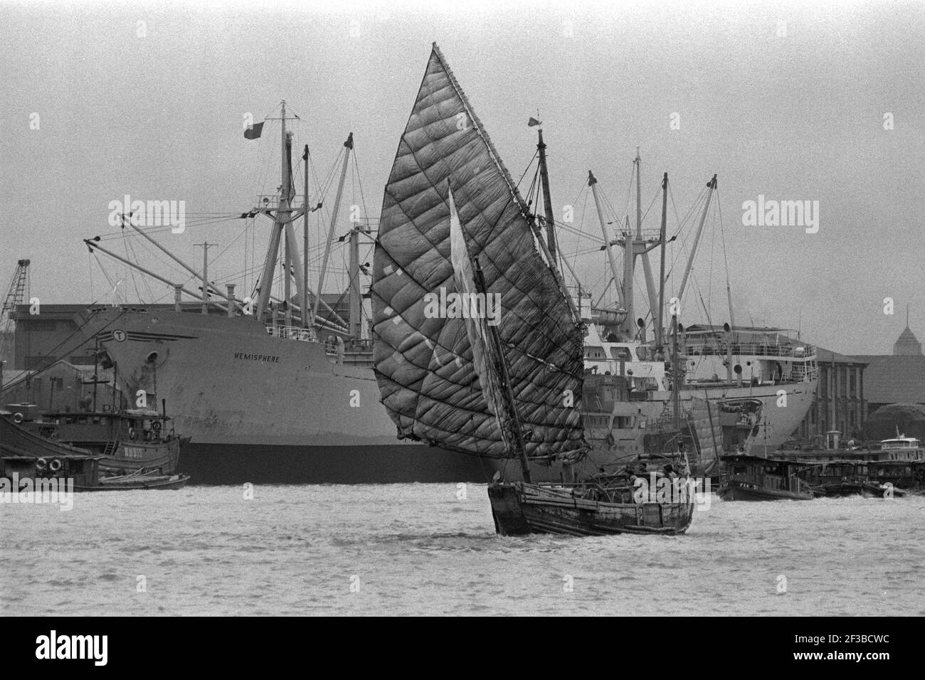 A junk in the port of Shanghai, in the background a motor cargo ship ...