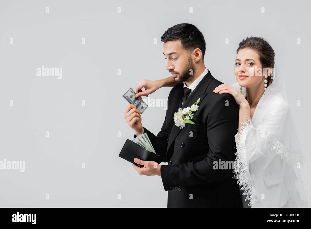 Smiling bride taking currency from muslim groom isolated on grey Stock ...