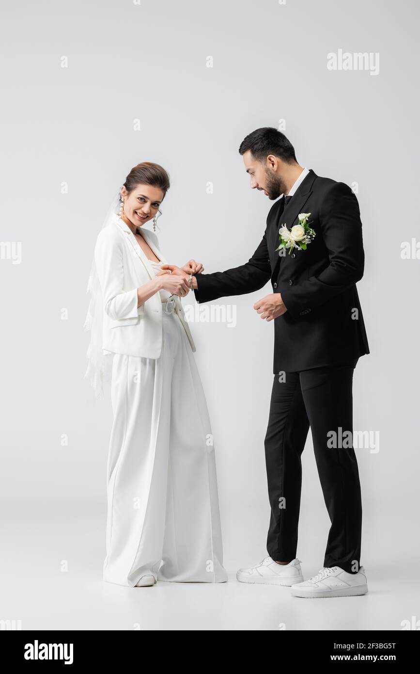 Cheerful bride wearing handcuffs on muslim boyfriend on white ...