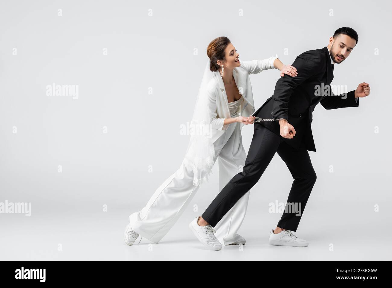 Arabian man in formal wear and handcuffs running near bride on white ...