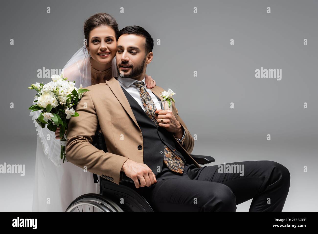 Smiling bride in wedding dress hugging arabian groom in wheelchair ...