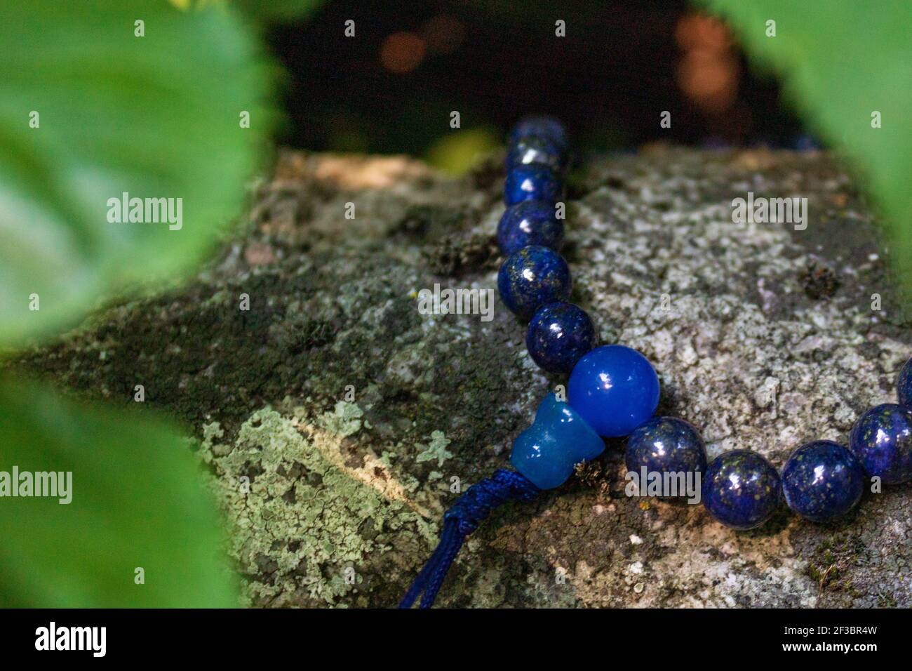Close up of blue mala beads on stone between green leaves. Buddhist ...