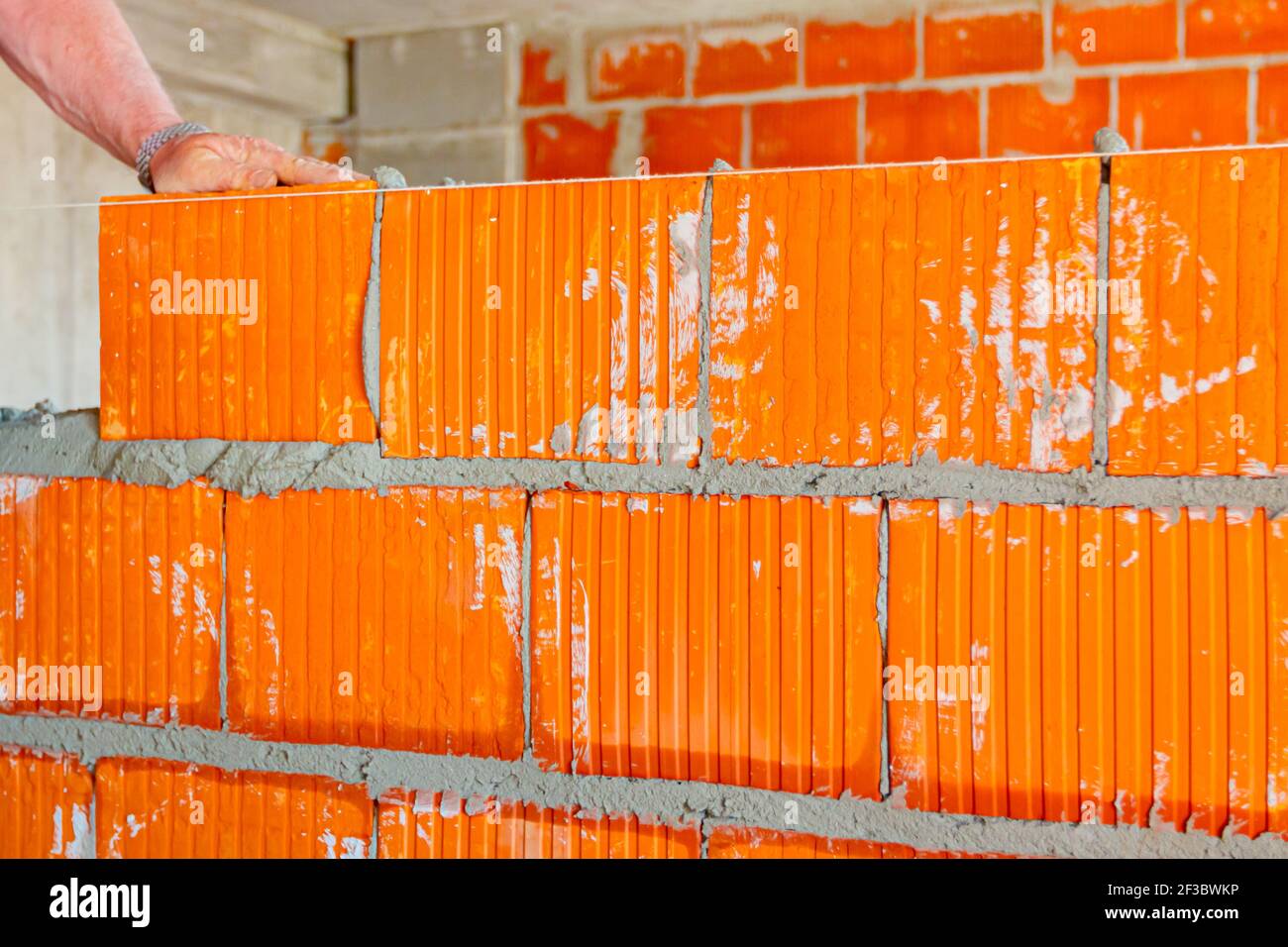 Mason, bricklayer worker is using red blocks to mount a wall next the ...