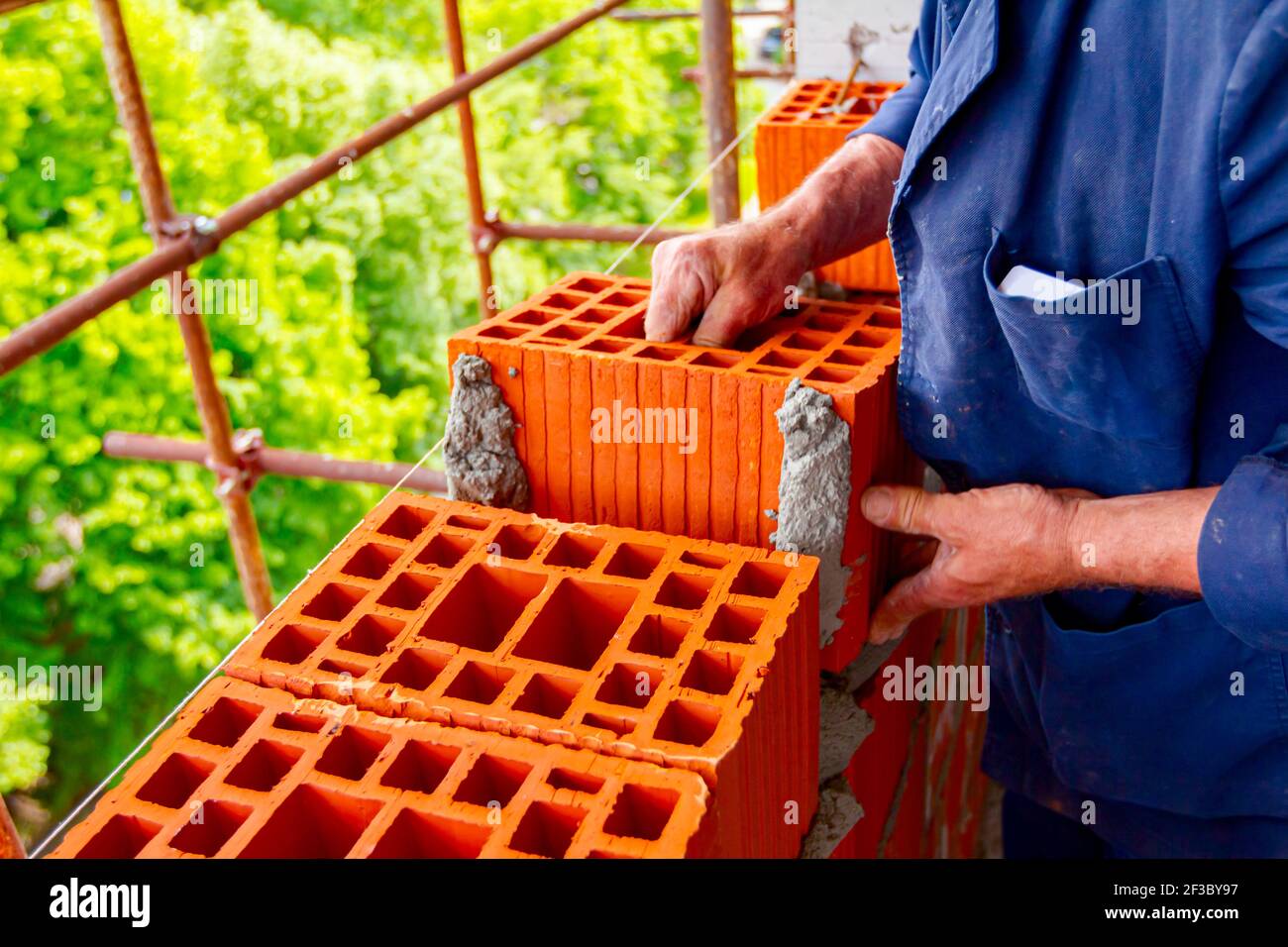 Mason, bricklayer worker is using red blocks to mount a wall next the ...