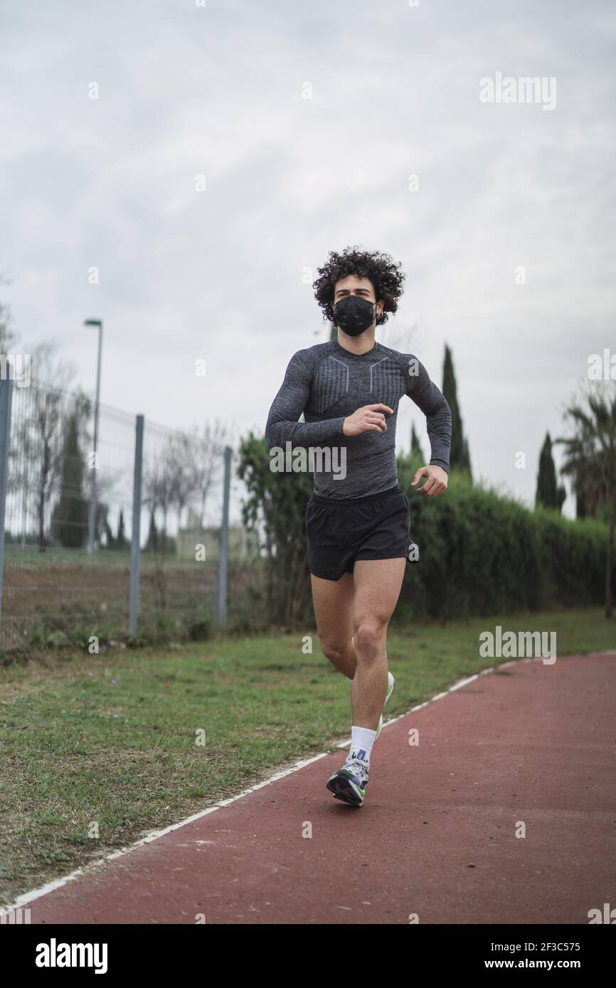 An energetic young Spanish male wearing a mask is running on the track ...