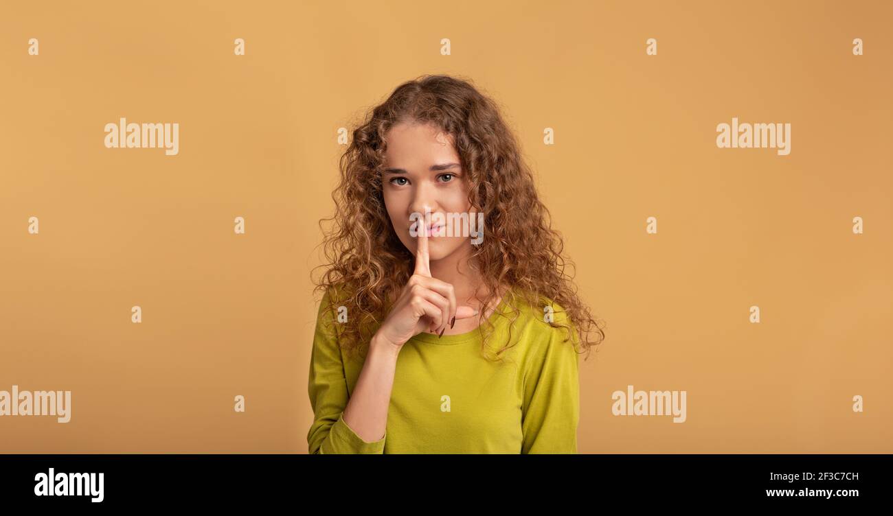 Cute red-haired curly girl teenager presses finger to lips, make silent ...