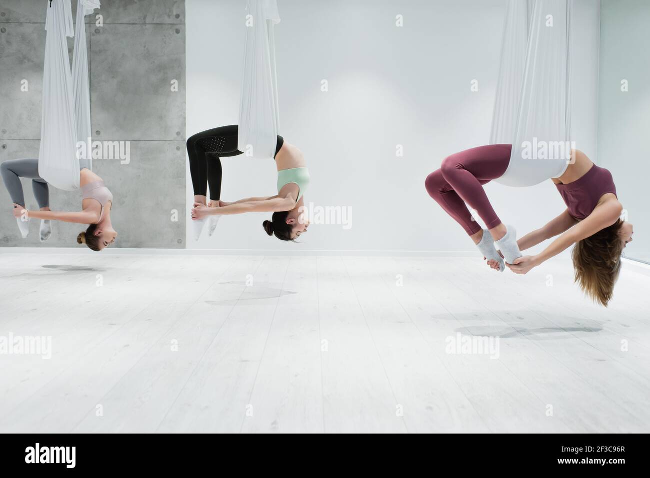side view of three young women practicing aerial yoga in gym Stock ...