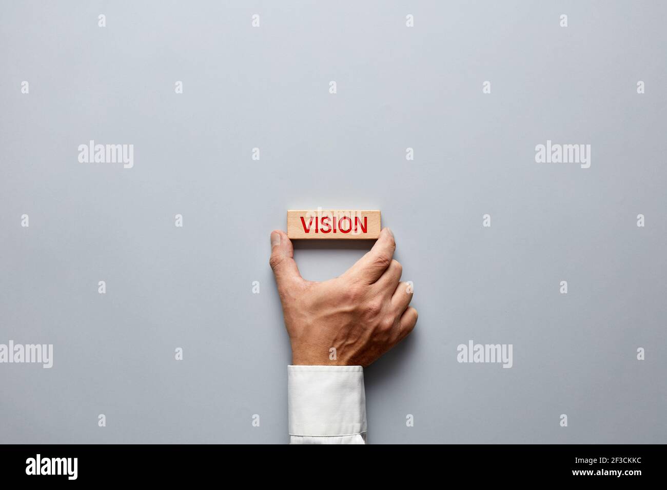 Businessman hand holding a wooden block with the word vision on gray ...