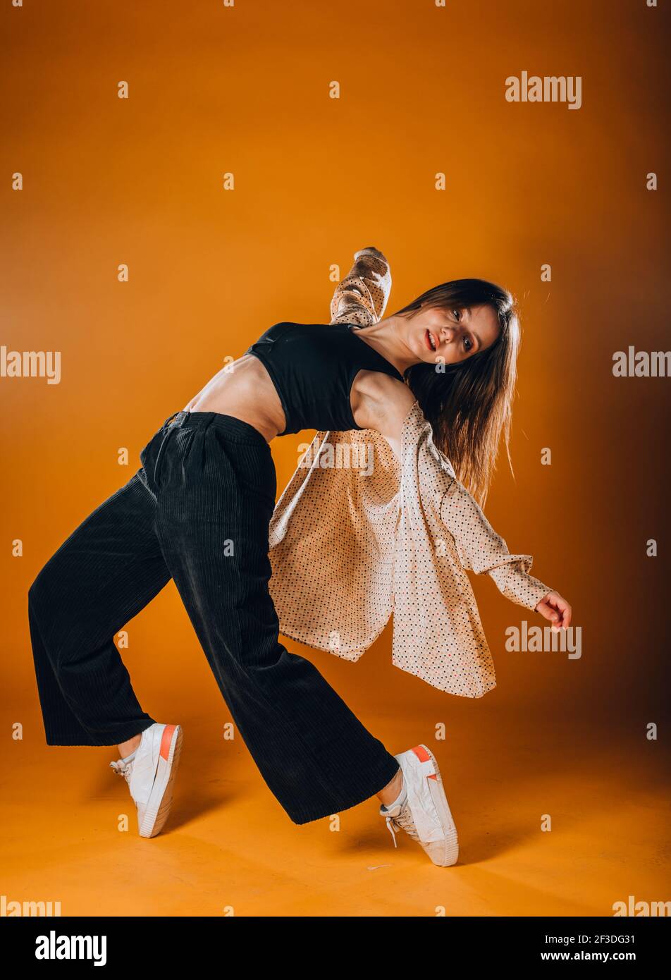 Fit young girl dancer performing a dance routine in the orange studio ...