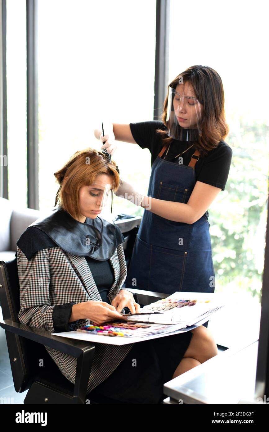 Asian female hairdresser make hairstyles for female customers in modern ...