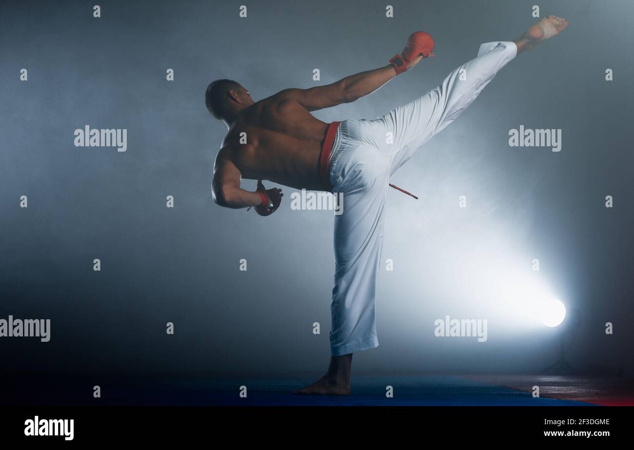 Male karate fighter performing kick isolated on dark background in the ...