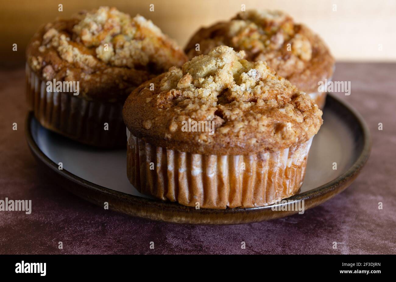Side view of three cinnamon crumb muffins on a plate atop a maroon ...