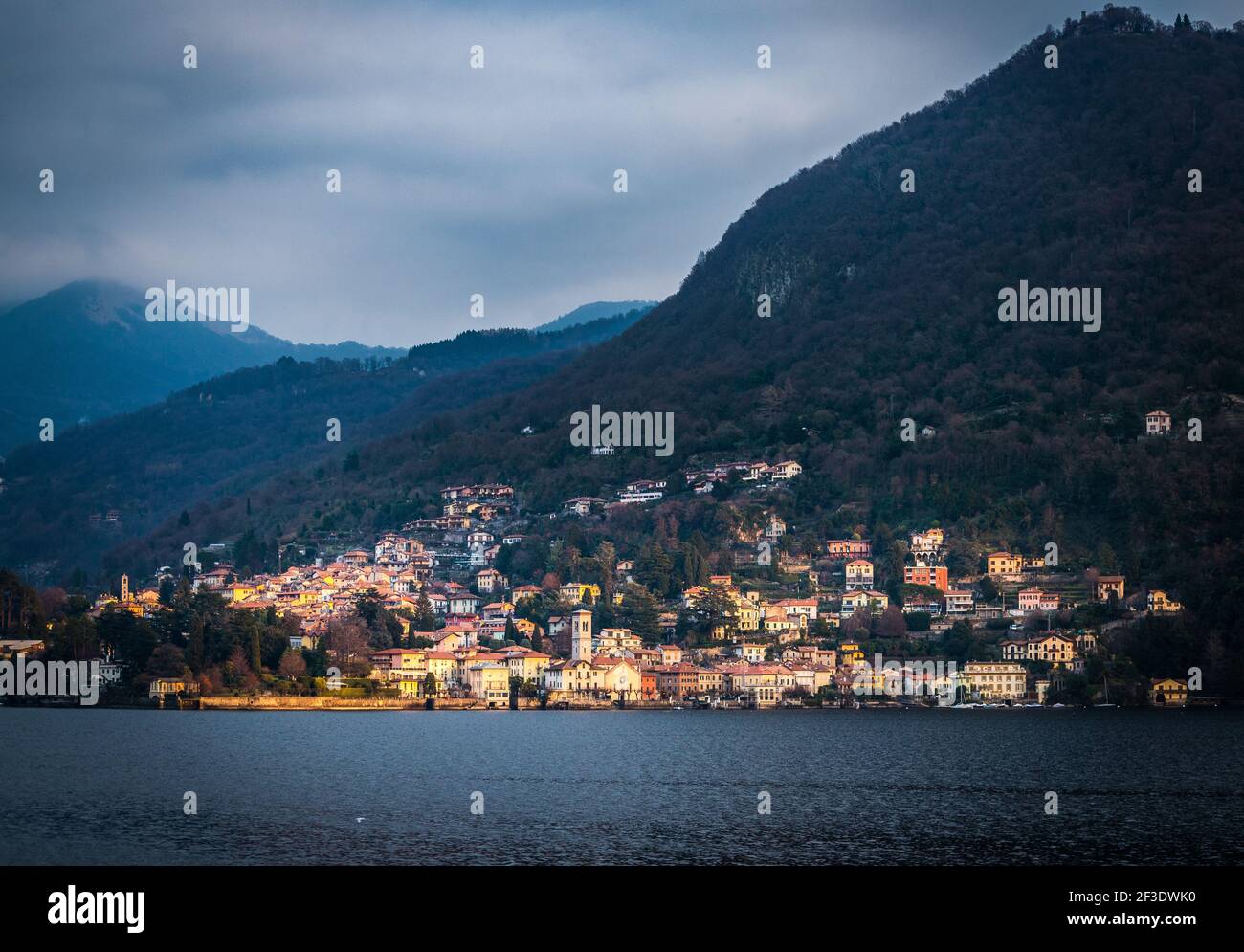 Buildings on opposite shore of lake. Wooded sharp hill above ...