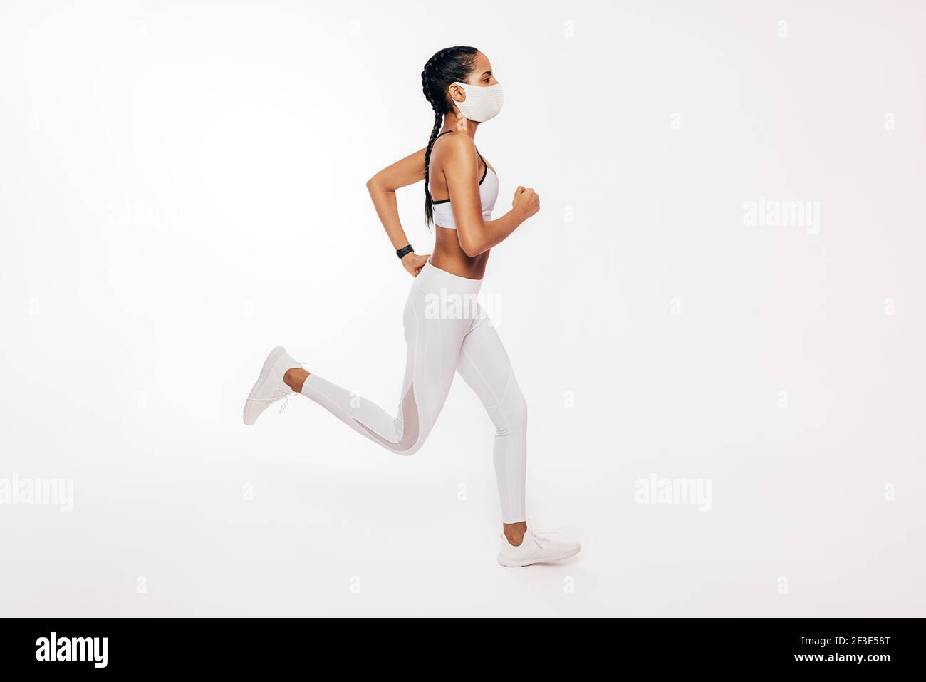 Side view of young fitness woman running over white background wearing ...
