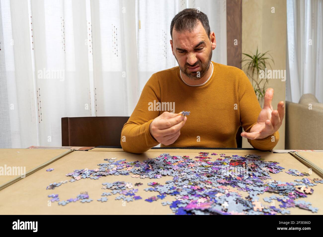 Handsome bearded man in an orange sweater doing puzzle with a worried ...