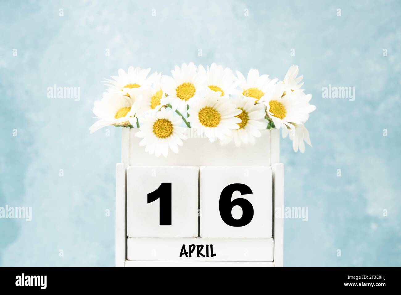 White cube calendar for April with daisy flowers over blue background ...