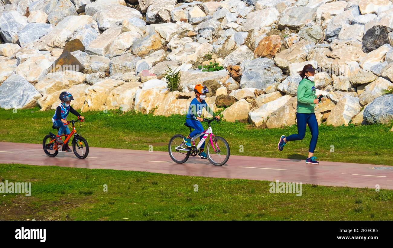Two children riding bicycles next to their mother who is running along ...