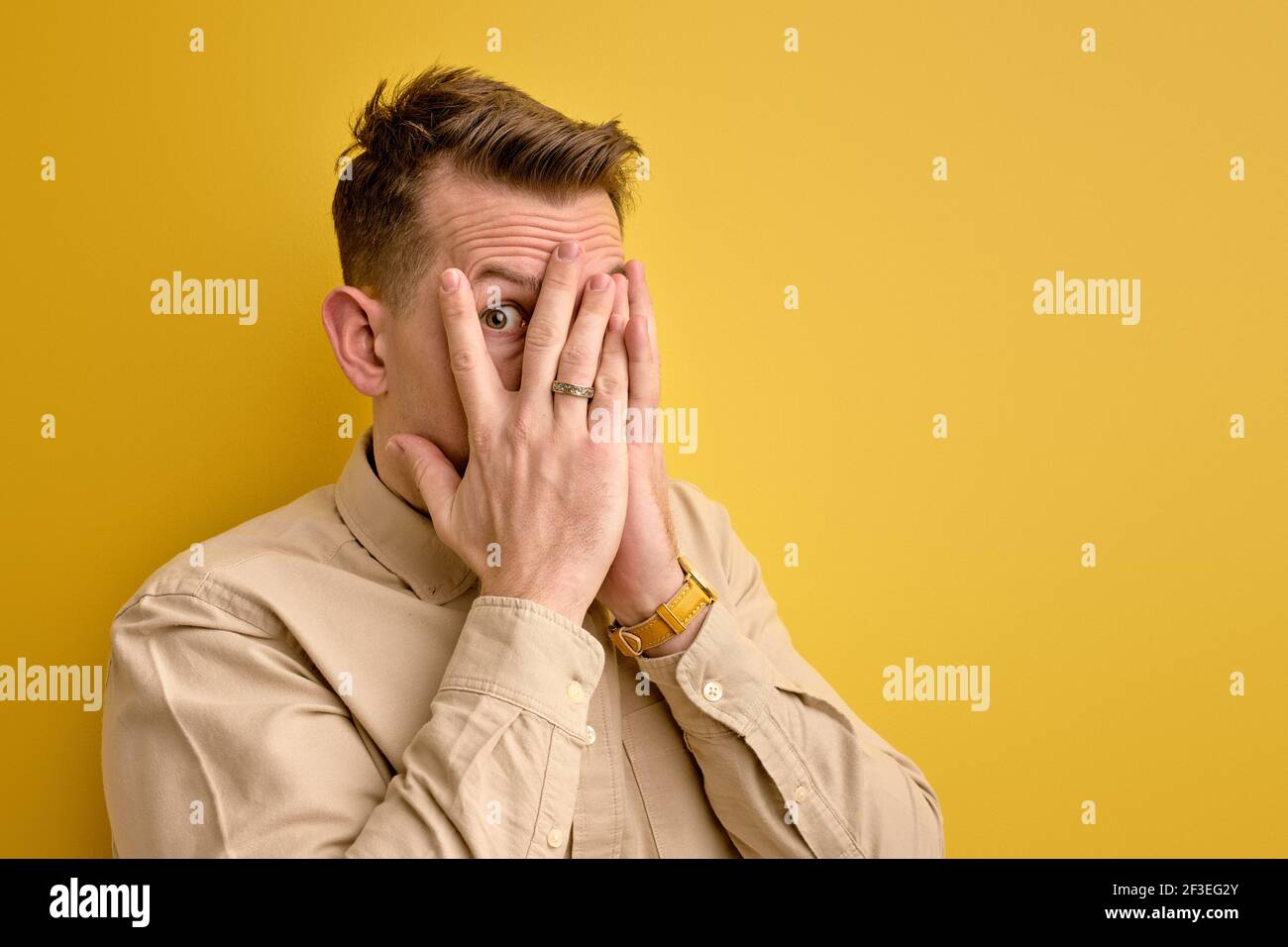 Scared man isolated over yellow background, closing face with hands ...