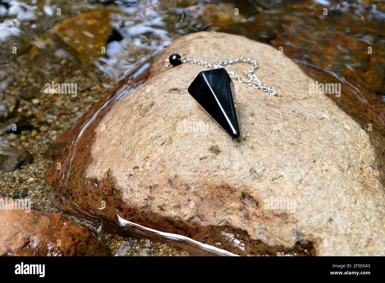 Black pendulum gem in onyx in front of a river Stock Photo - Alamy