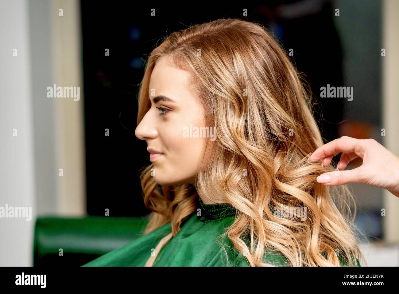 Side view of hands of female hairdresser styling hair of a blonde woman ...