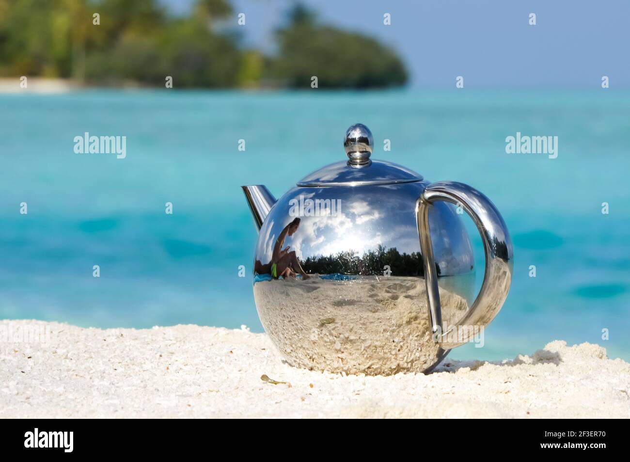 stainless steel teapot on a tropical beach. a blurred island with palm ...