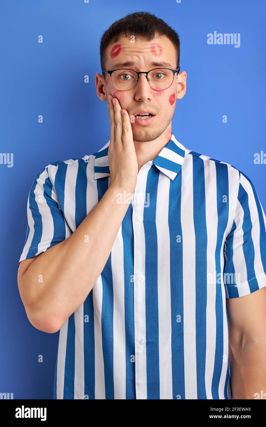 disheveled young man with traces of kiss on cheek look at camera in ...