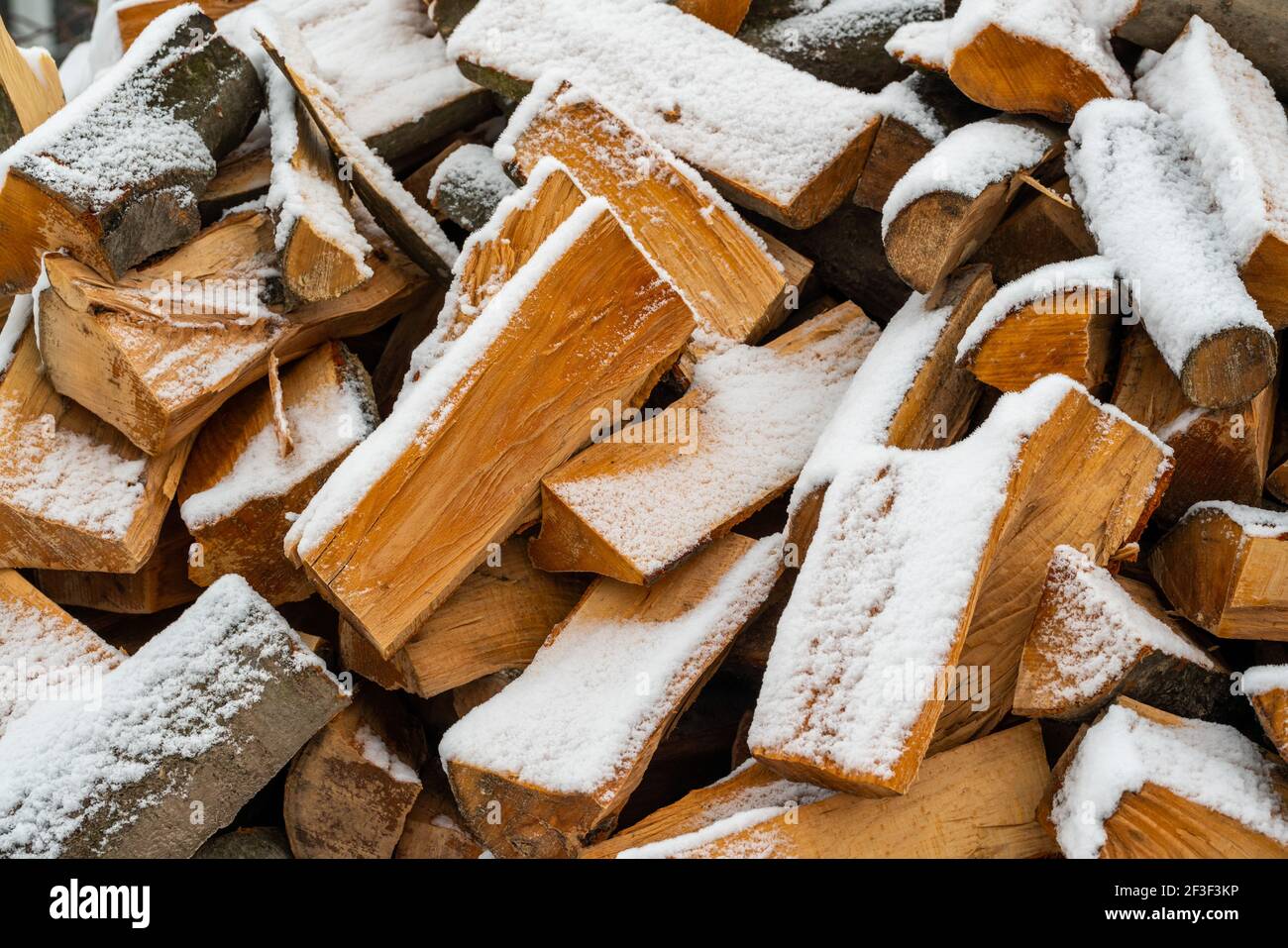 Stacked firewood covered with snow. A woodpile of dry fire woods in the ...