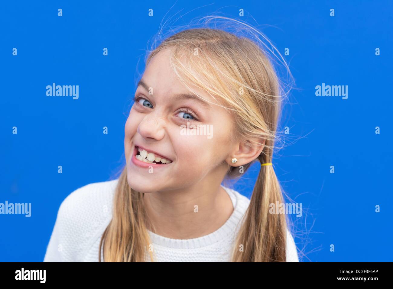 Cute young girl making funny face over blue background. Copy space ...