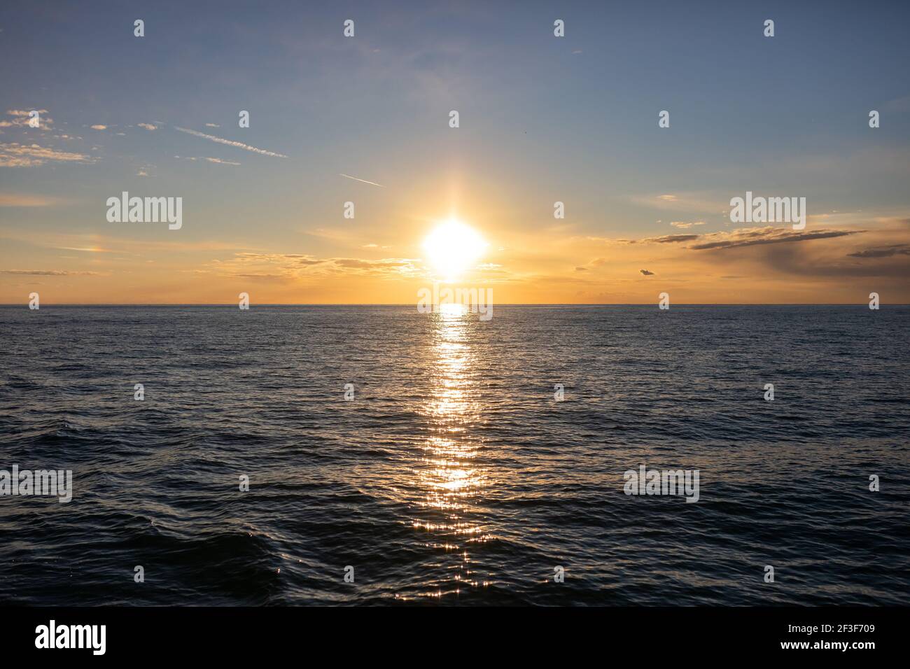 The wavy ocean gleaming under the sunset piercing through the clouds ...