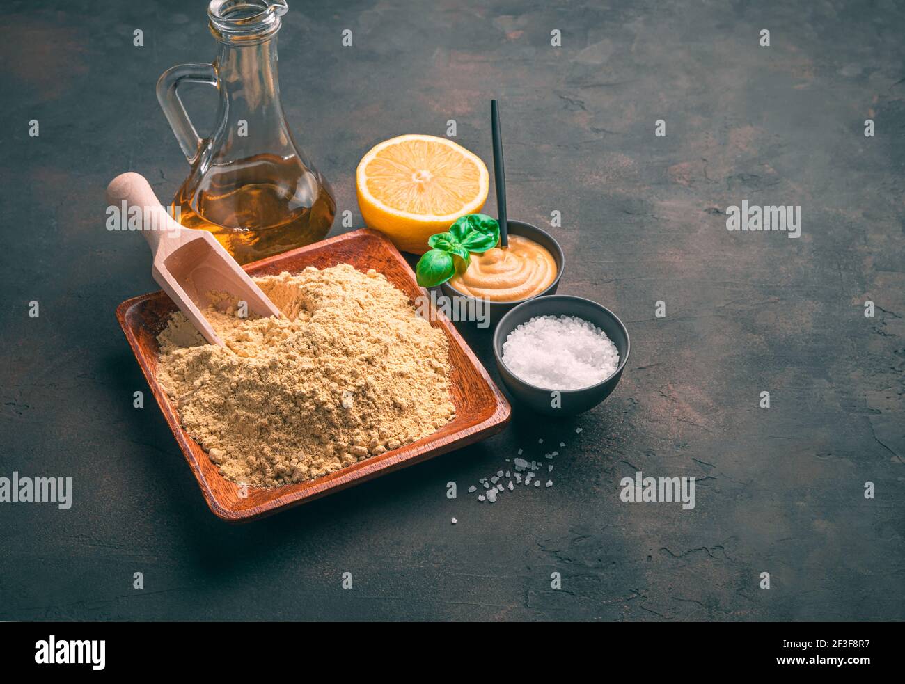 Mustard powder, ready-made mustard, salt, lemon and oil on a brown ...