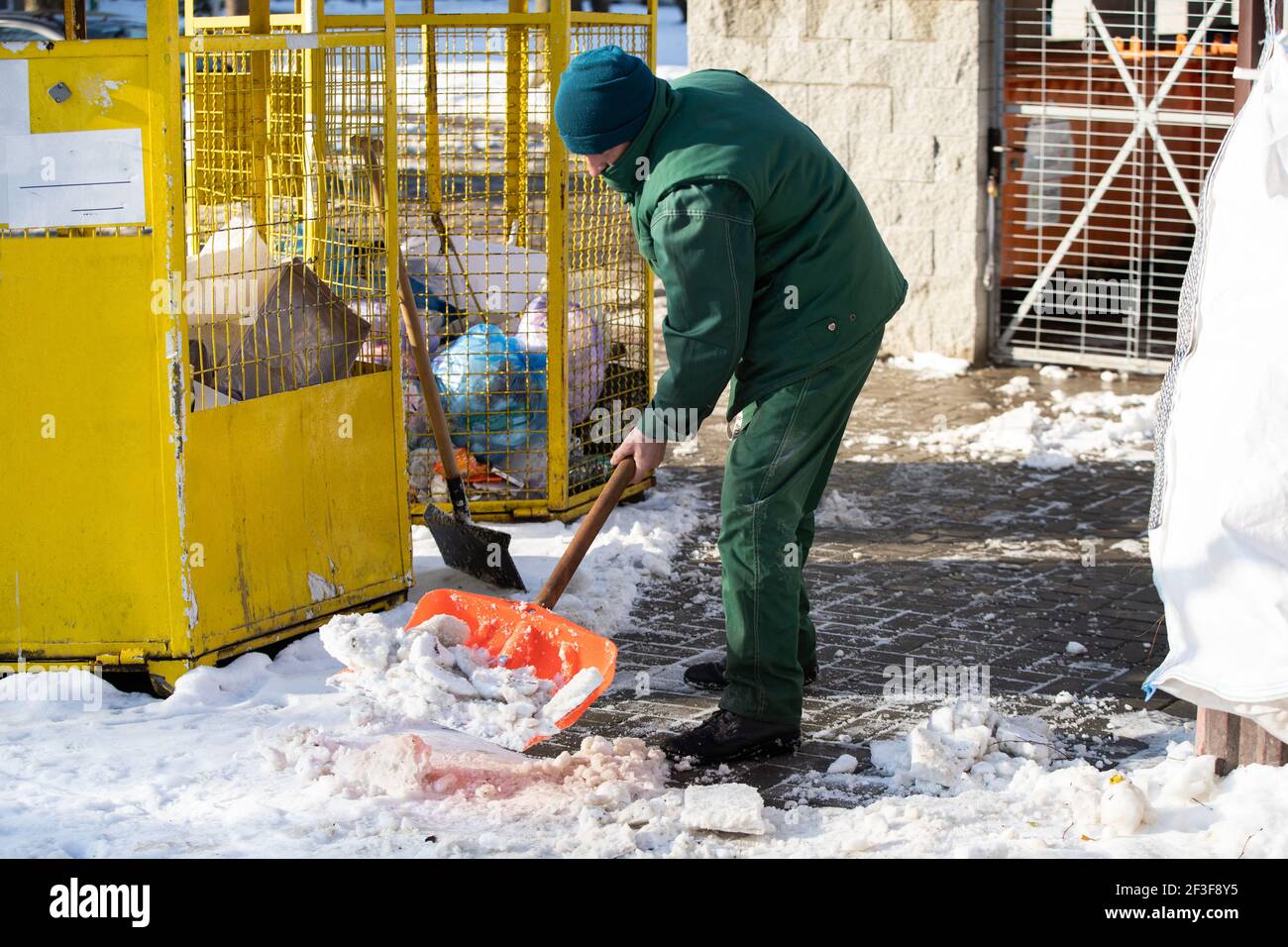 A manual worker scoops snow from the pavement and shovels it onto a ...