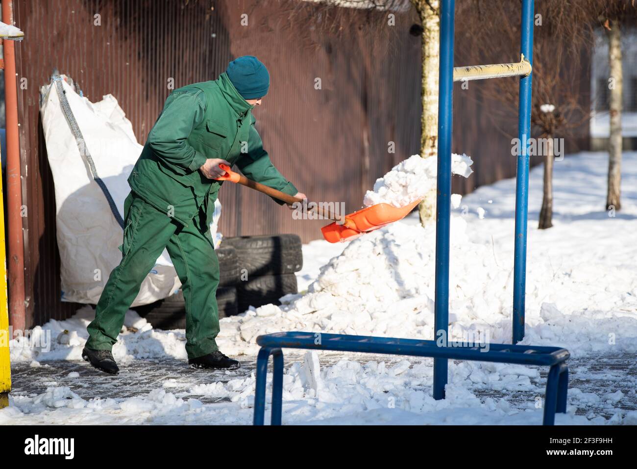 A manual worker scoops snow from the pavement and shovels it onto a ...