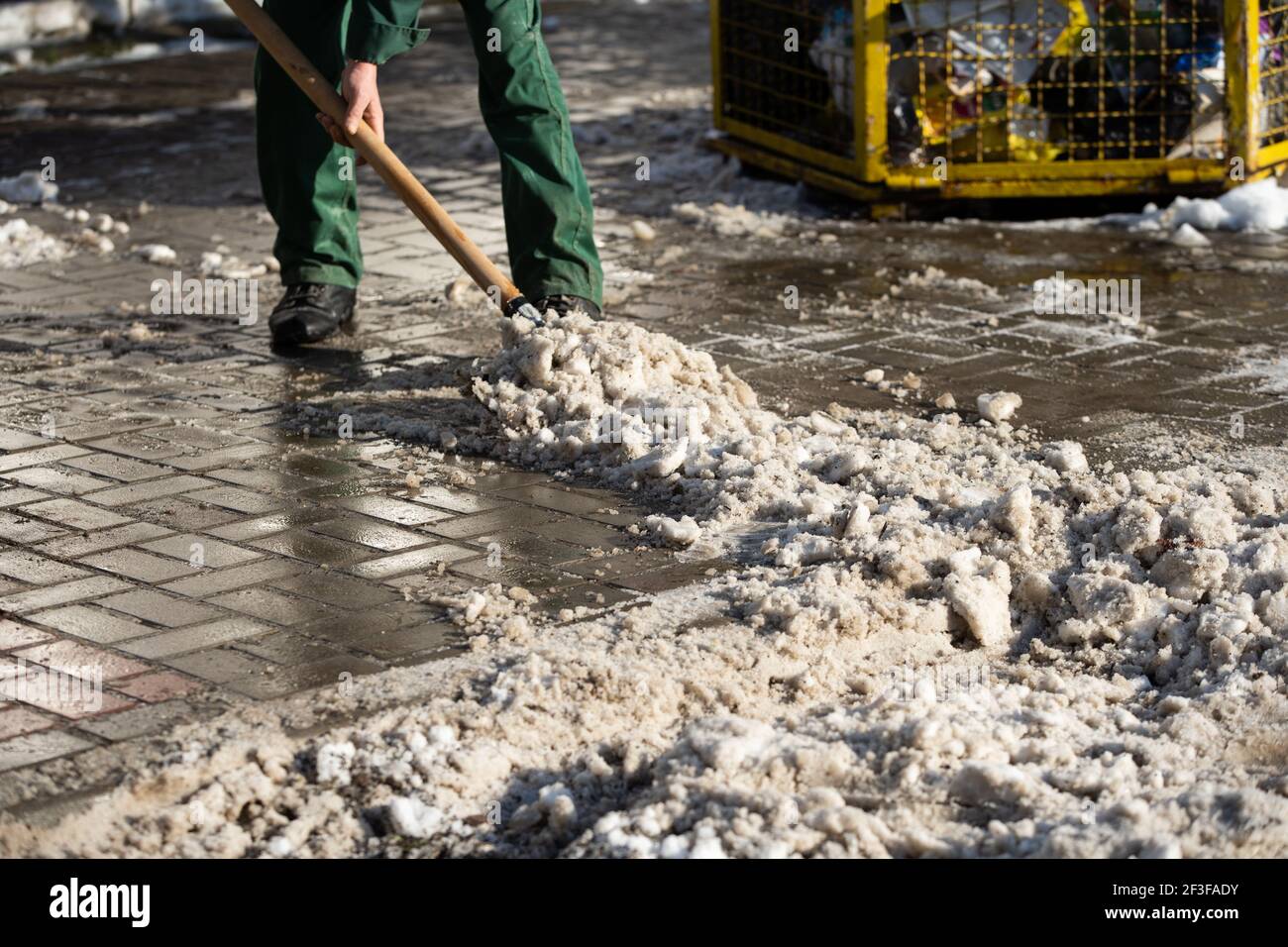A manual worker scrapes snow off the pavement with a metal shovel Stock ...