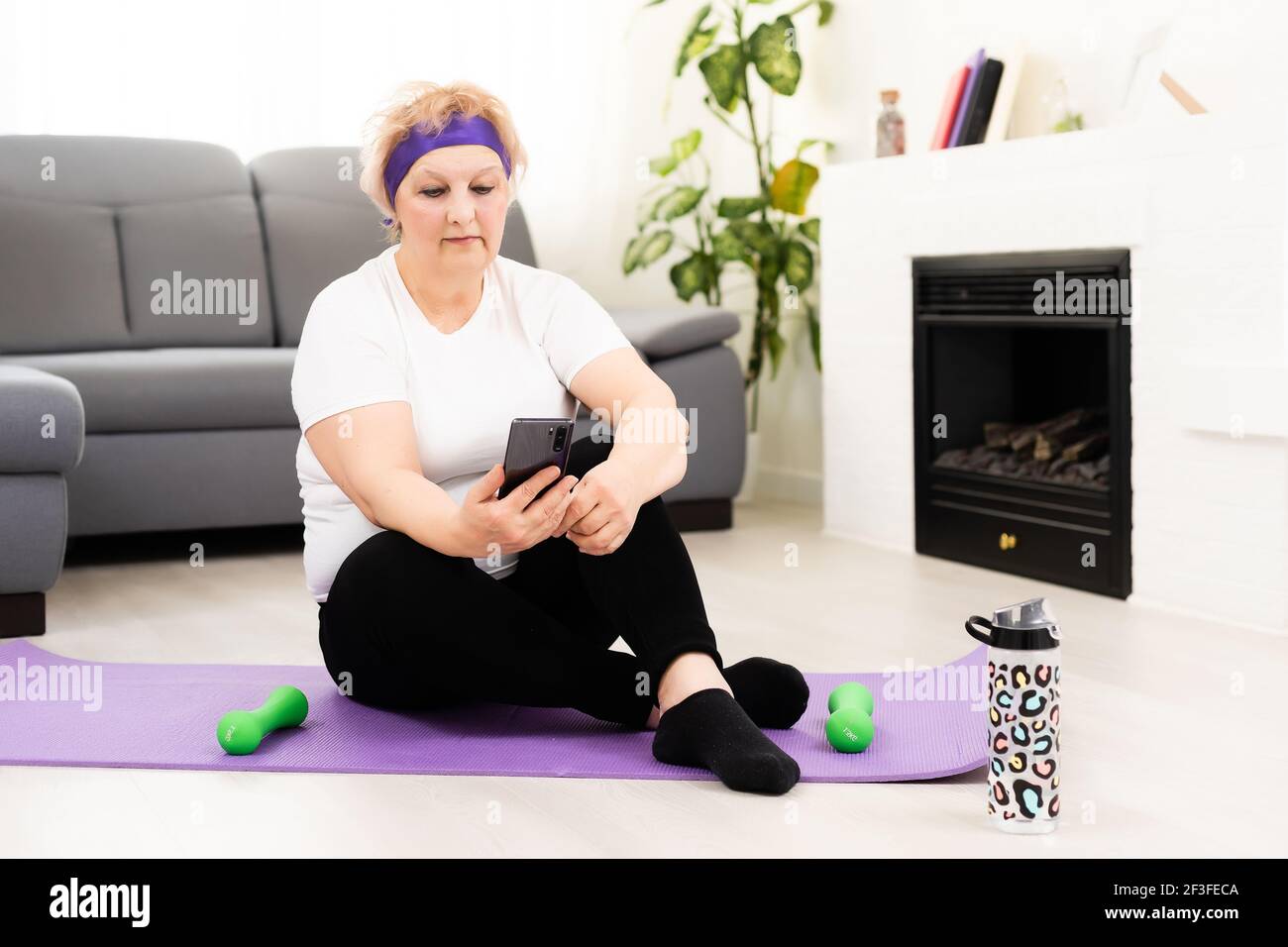 older woman training gym at home holding smartphone. Senior female ...