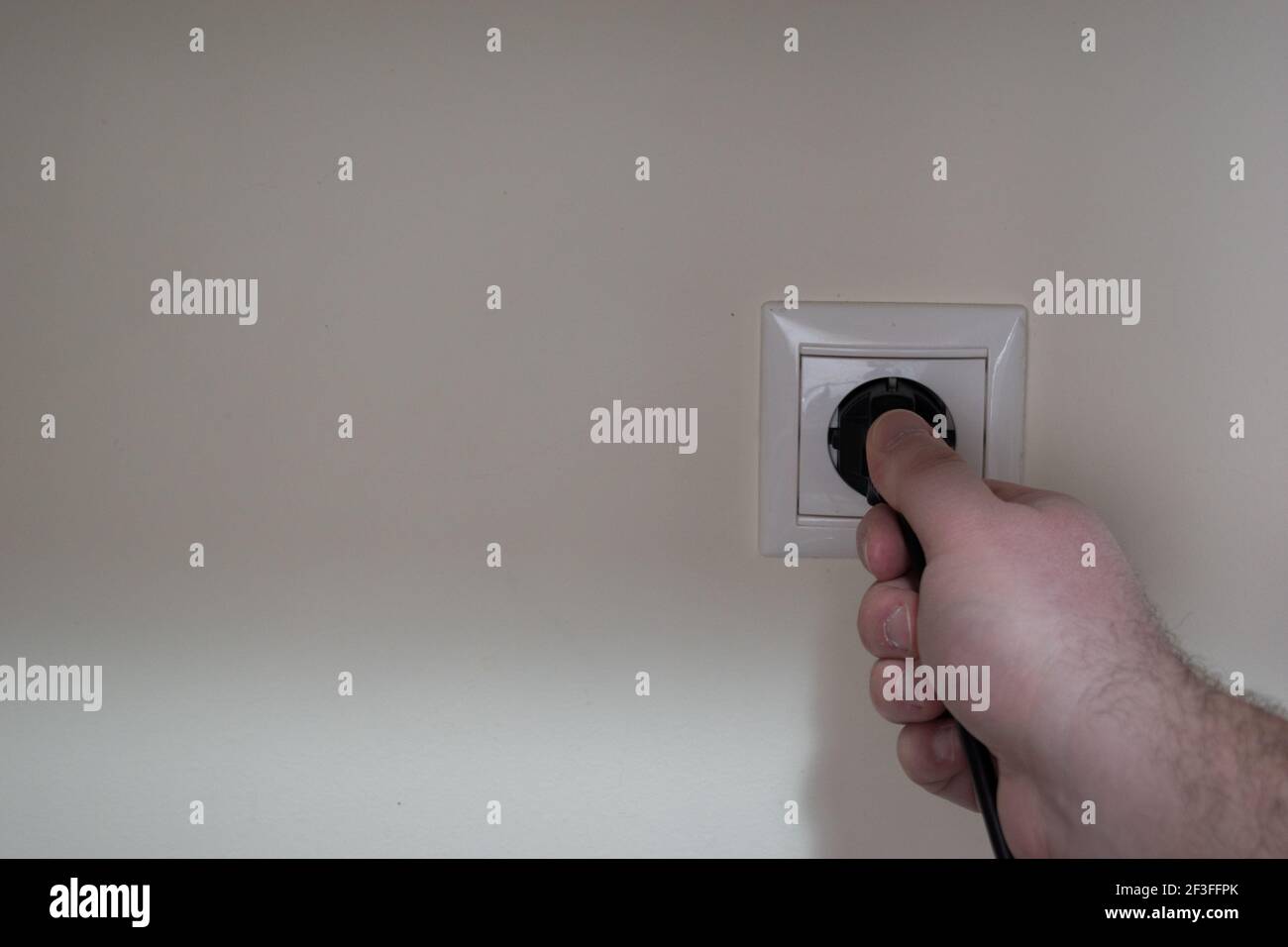 A male hand is pulling one black electrical cord plugged into a wall ...