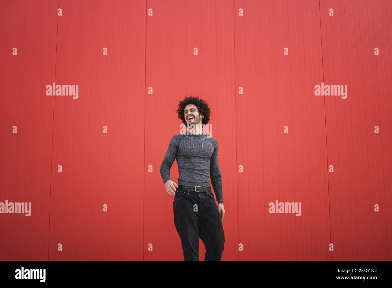 A happy stylish Spanish guy with curly hair posing in the red wall ...