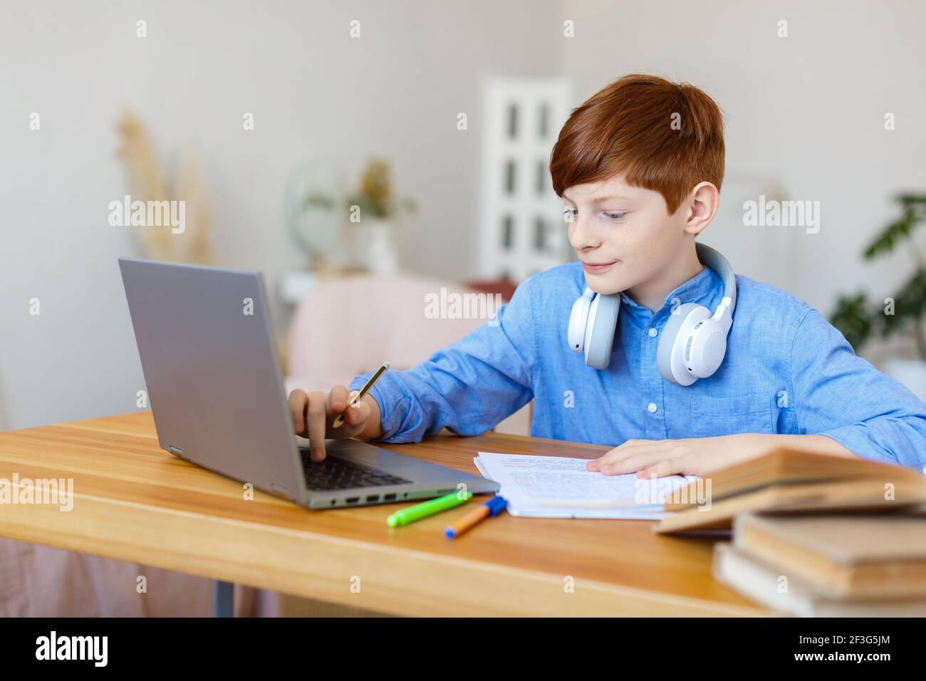 Smiley teenager boy doing homework at home in front of a laptop monitor ...