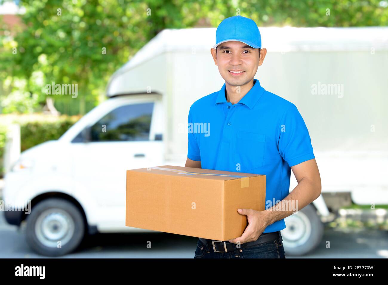 Deliveryman carrying a cardboard parcel box in front of delivery car ...