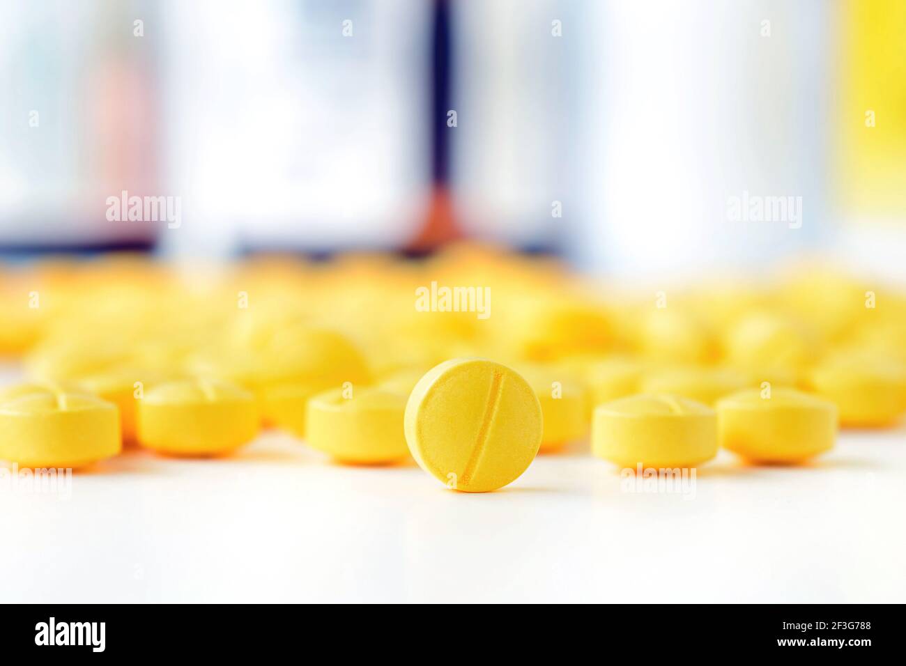 Heap of small yellow tablets (or pills) on white table with blur ...