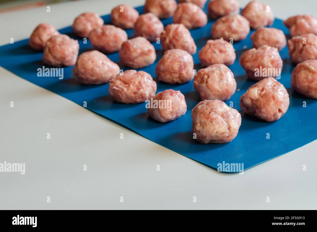 Raw shaped meatballs on blue. Rows of meatballs with pepper, salt and ...