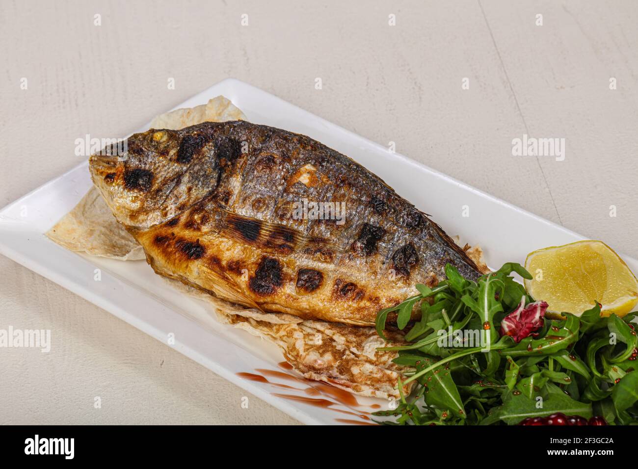 Grilled dorada fish served lemon and rucola Stock Photo - Alamy