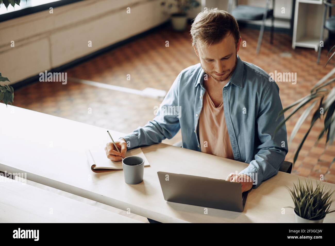 Young businessman making notes in notepad while sitting at the working ...