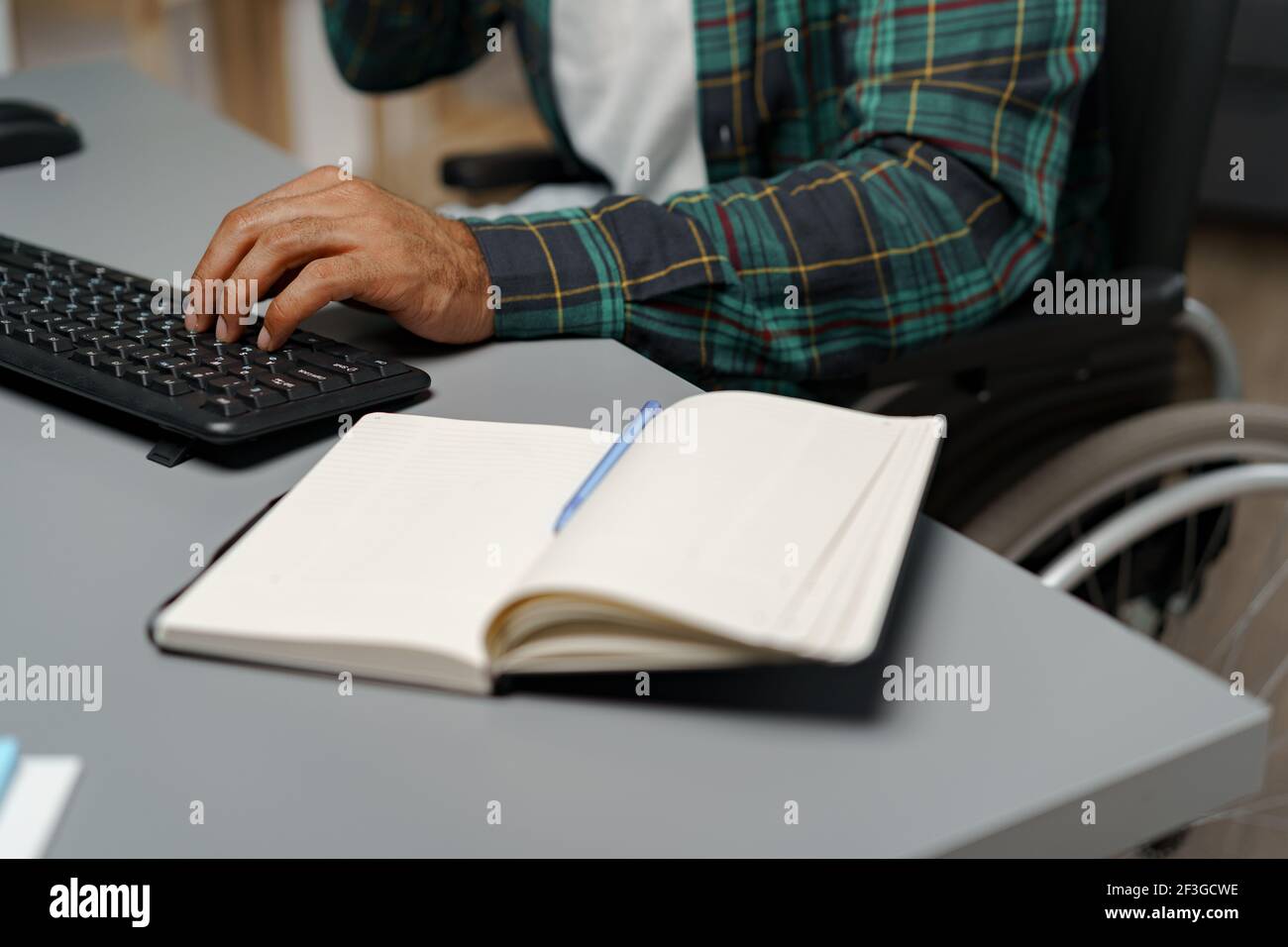 Disabled young african american man in wheelchair using computer while ...